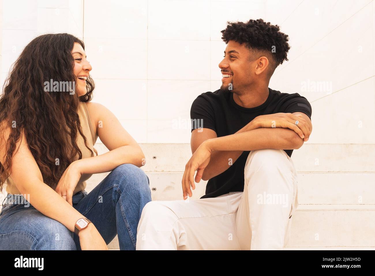Smiling young couple talking while sitting on steps Stock Photo - Alamy