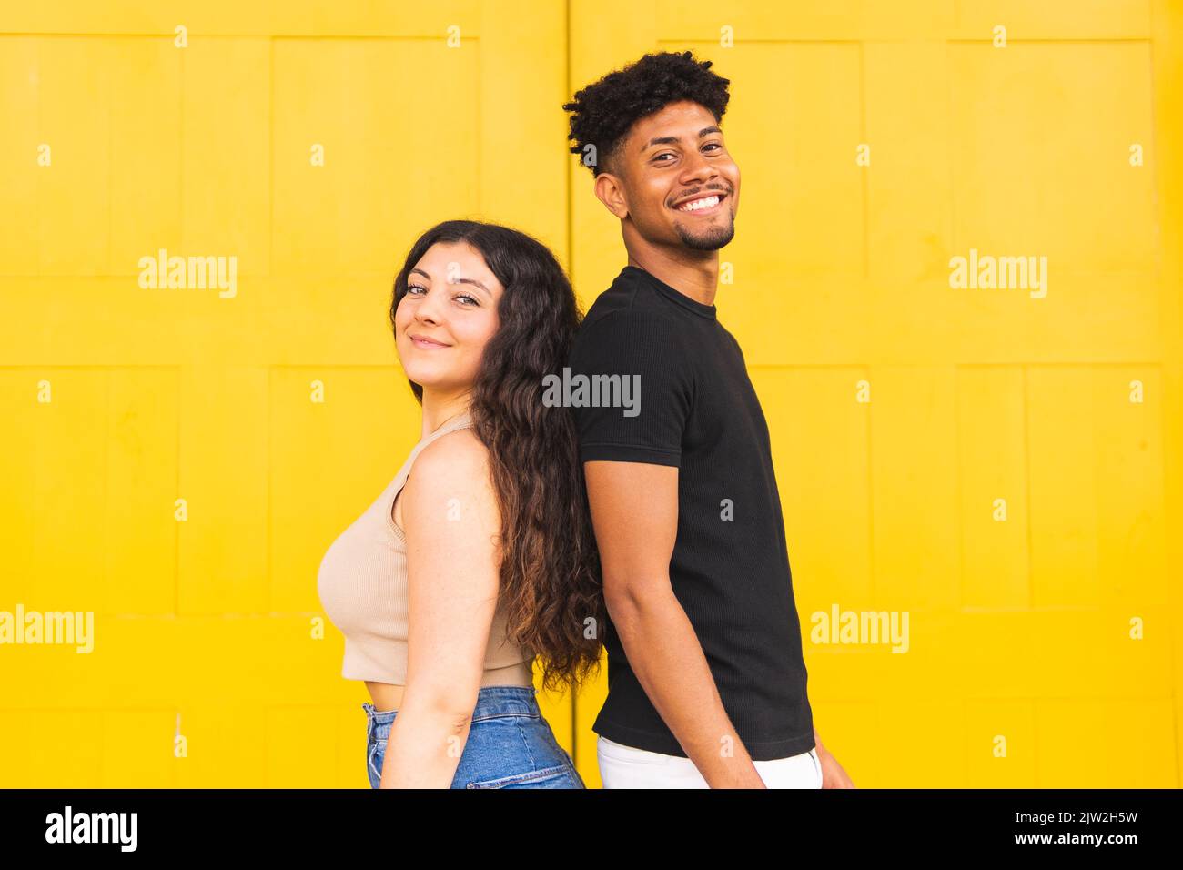 Portrait of confident young couple standing back to back against yellow ...