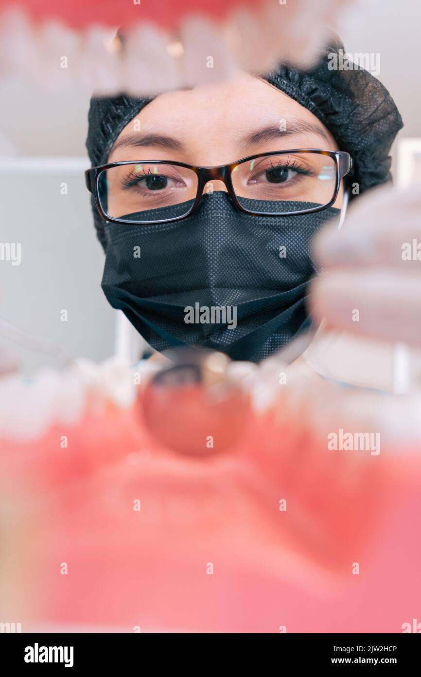 Concentrated young female medic in sterile mask gloves and eyeglasses ...