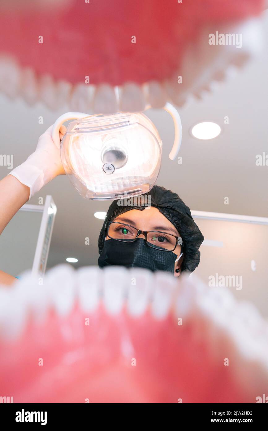 Low angle of attentive young female dentist in mask cap and eyeglasses ...