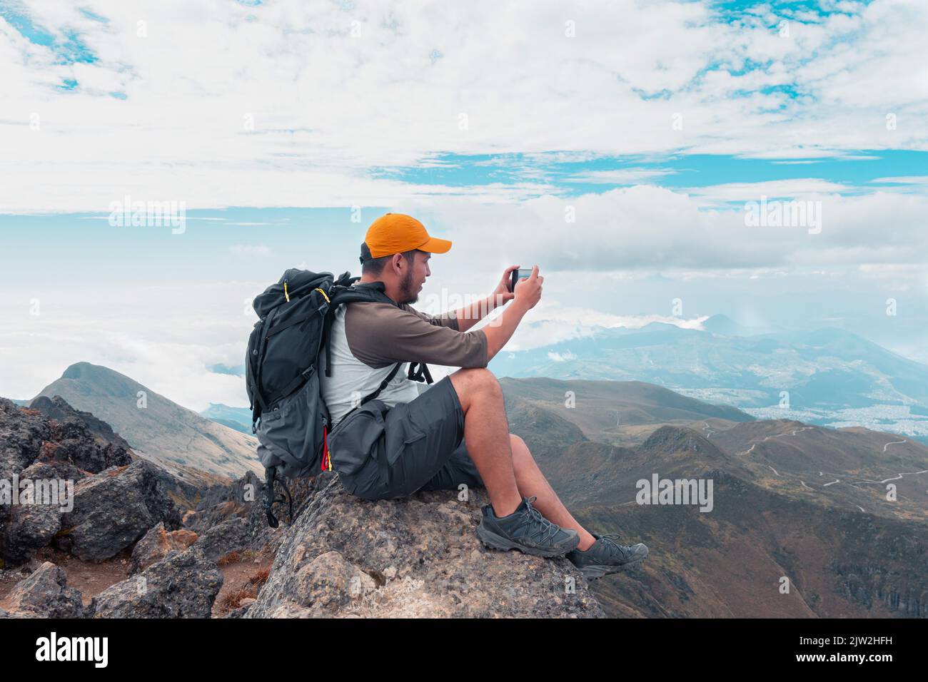 Side view of male traveler sitting on edge of rocky cliff and taking ...