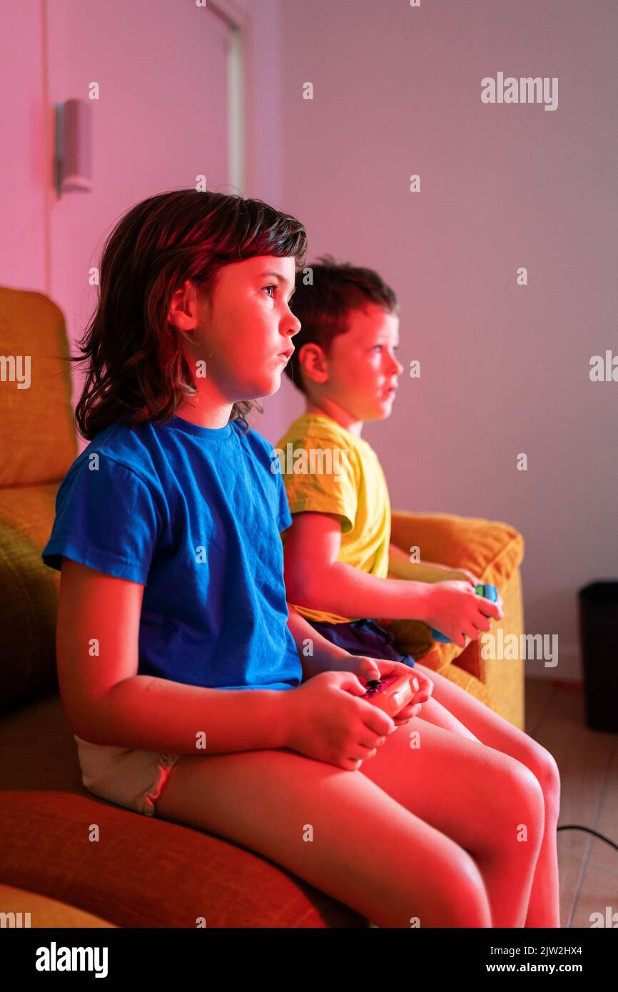 Side view of focused siblings with game pads playing video game while ...