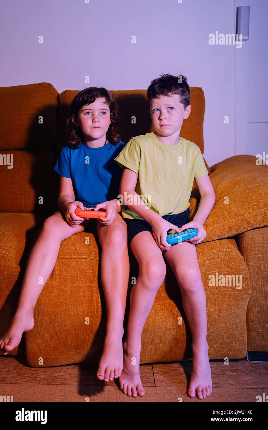 Full body of focused siblings with game pads playing video game while ...