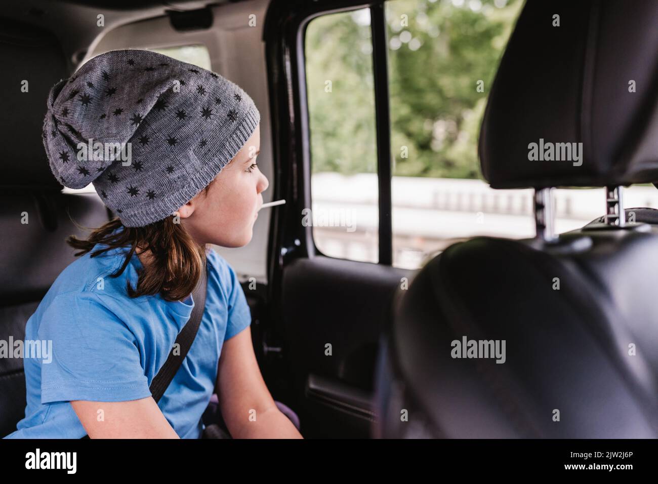 Kid with lollipop sitting on back seat of car and looking out window ...