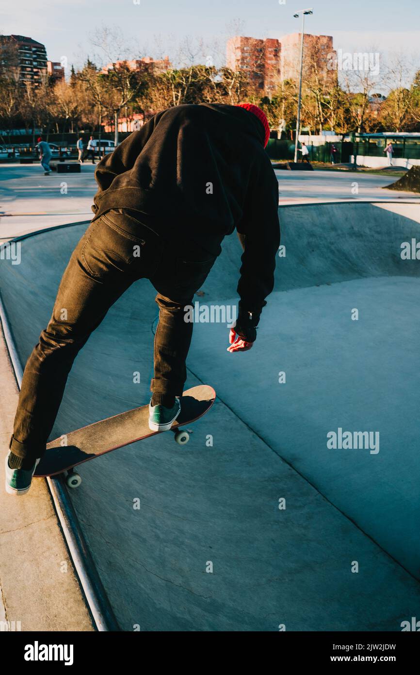 Back view of man balancing on skateboard on edge of ramp while ...