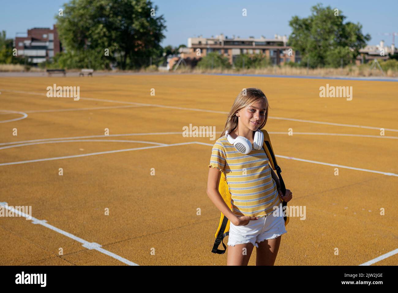 Teenage girl in shorts with yellow backpack standing looking at camera ...