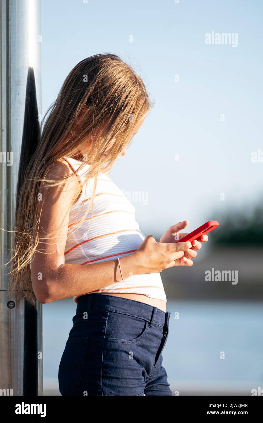 Side view of girl texting message on cellphone while standing on paved ...