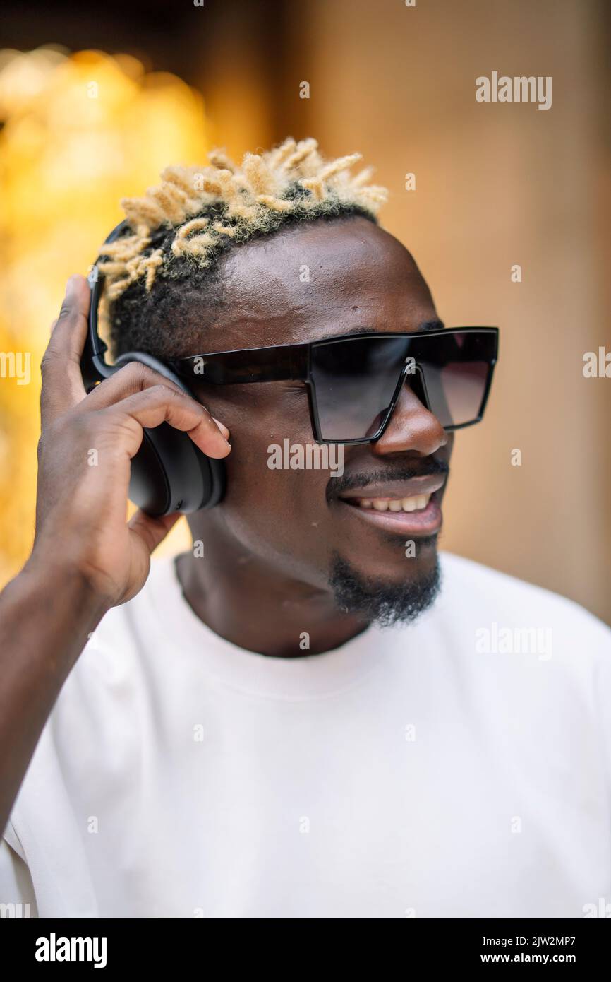 Glad African American male meloman in t shirt and sunglasses adjusting ...