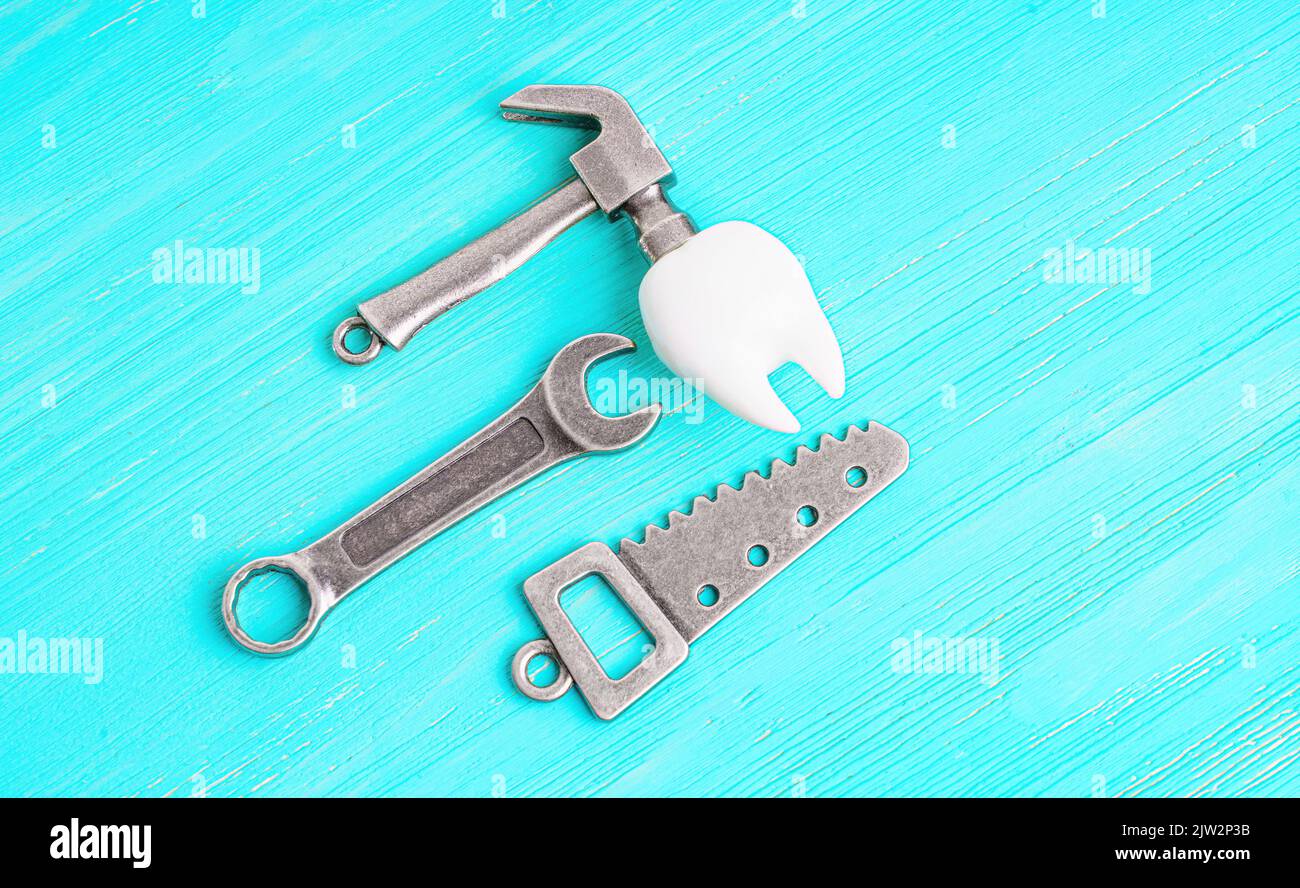 Human tooth model, steel hammer, wrench and handsaw on a blue wooden ...