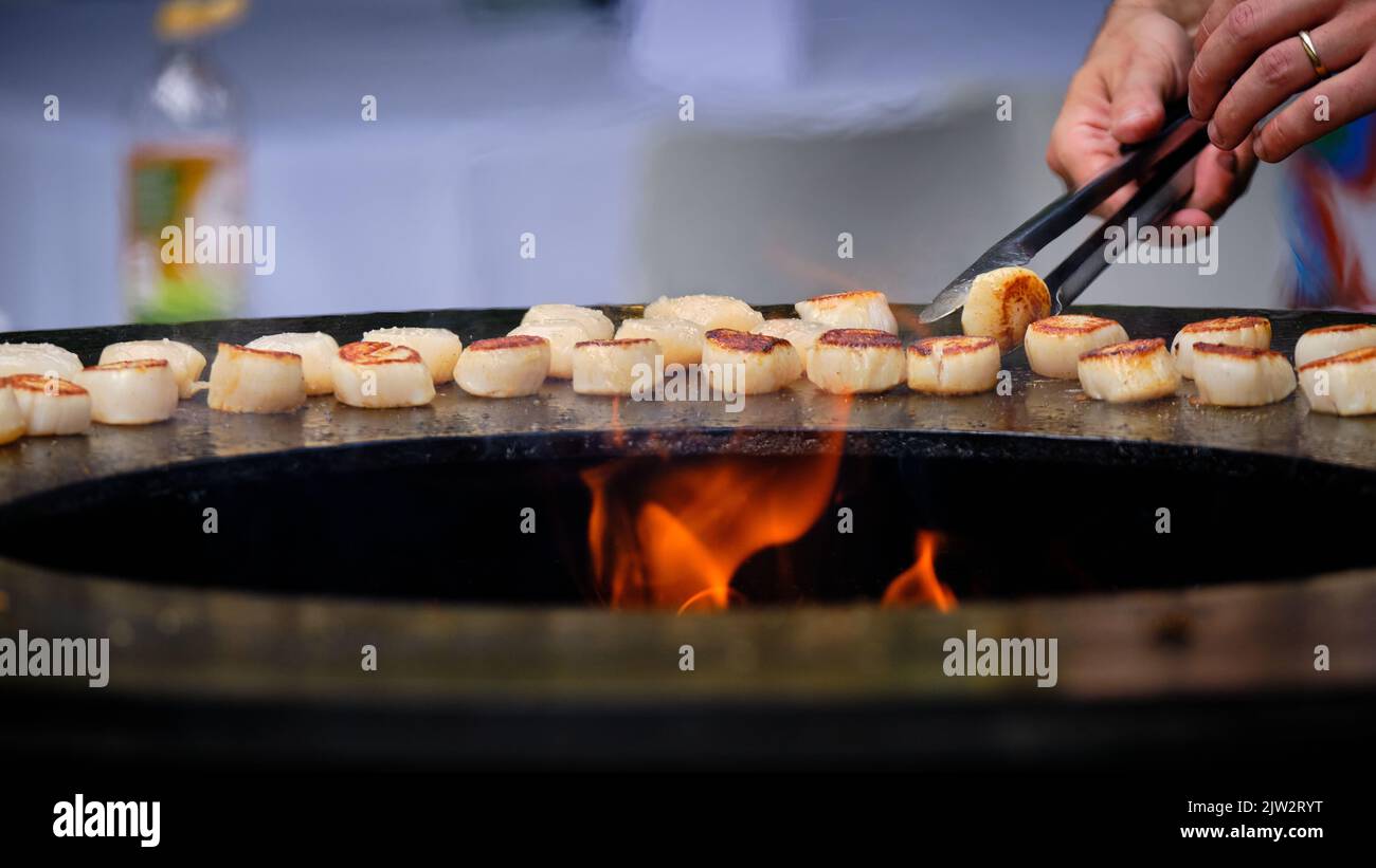 Delicious scallops being flipped over grilling on round steel iron ...