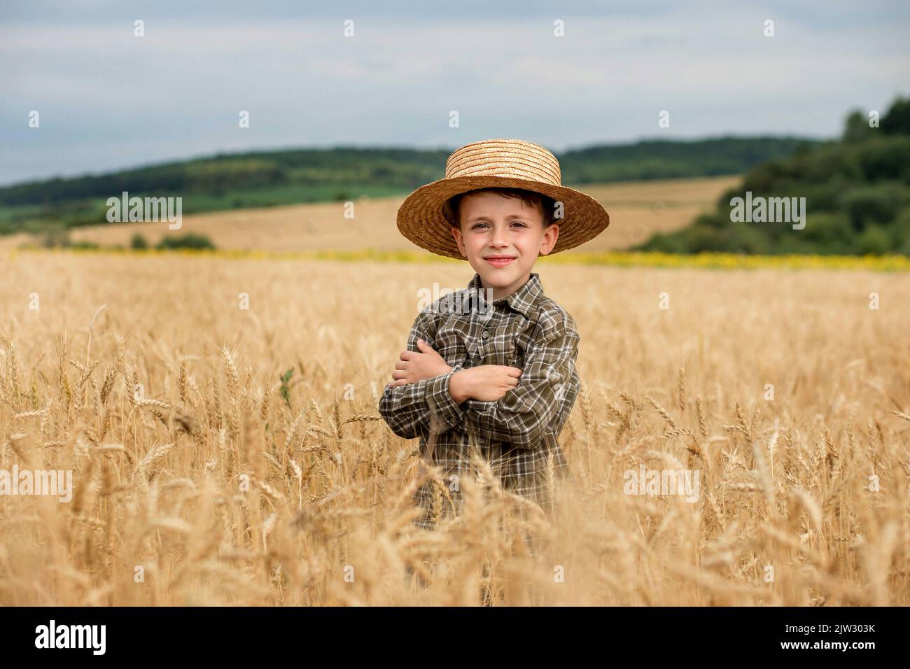 A smiling little farmer boy in a plaid shirt and straw hat poses for a ...