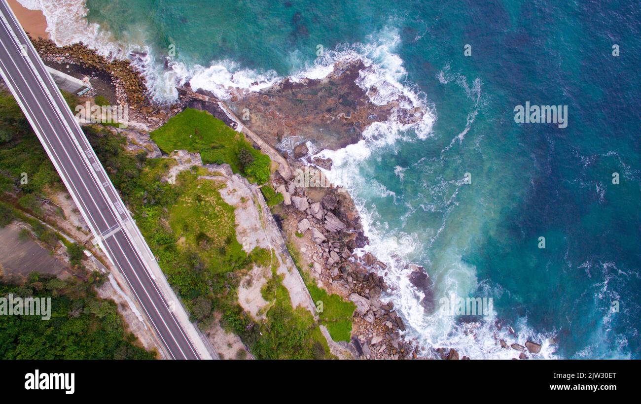 A scenic aerial view asphalt road by the sea with the waves hitting the ...