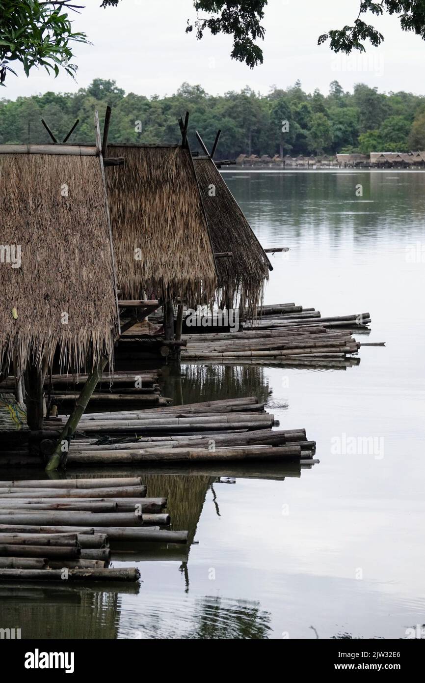 A vertical shot of thatched huts on the bench with trees on the water ...