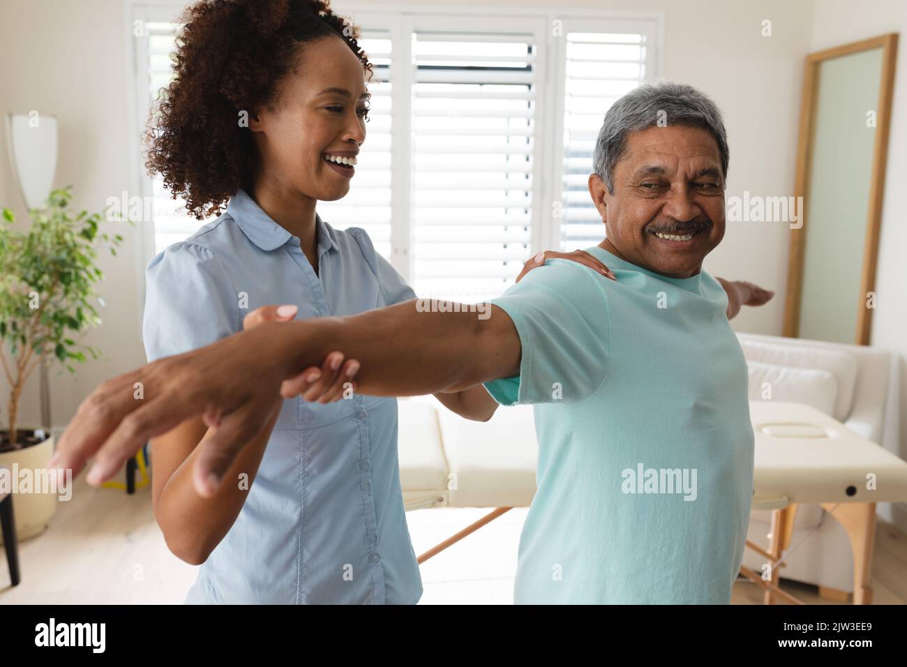 Mixed race female physiotherapist helping senior man stretching his arm ...