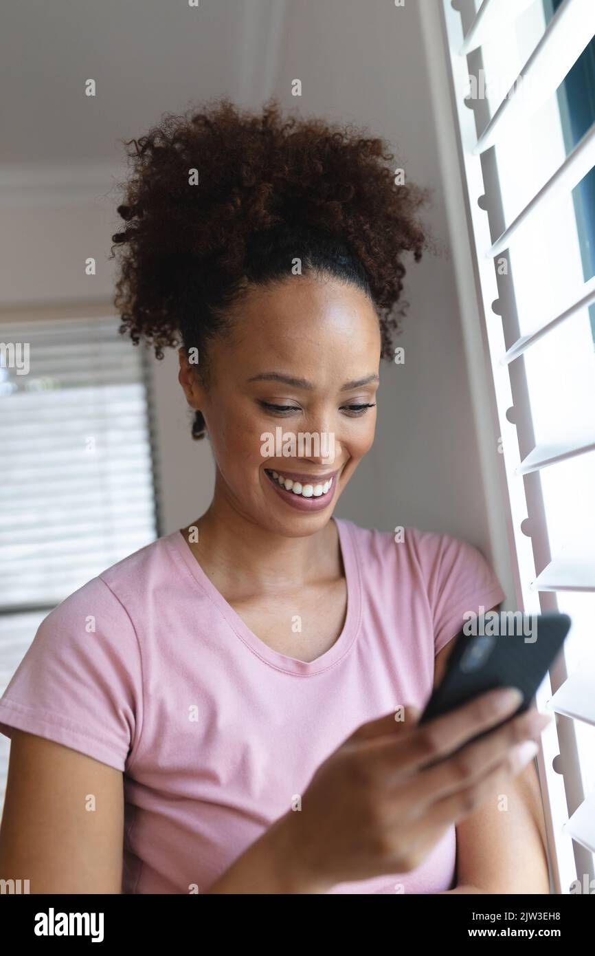Mixed race woman standing next to window using smartphone Stock Photo ...