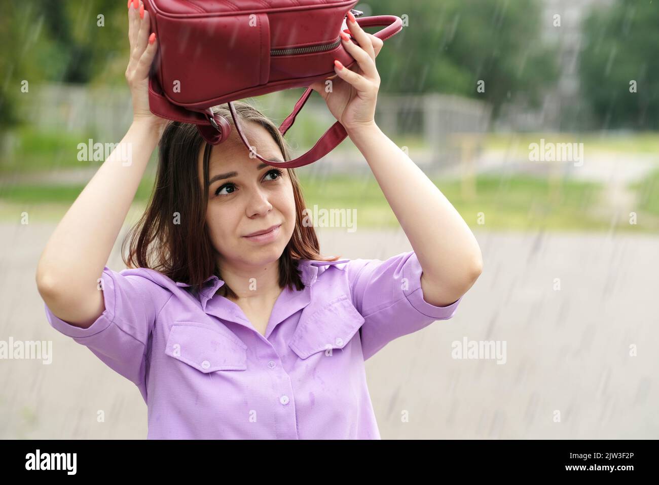 Young woman on street in rain. Positive female in purple shirt holding ...