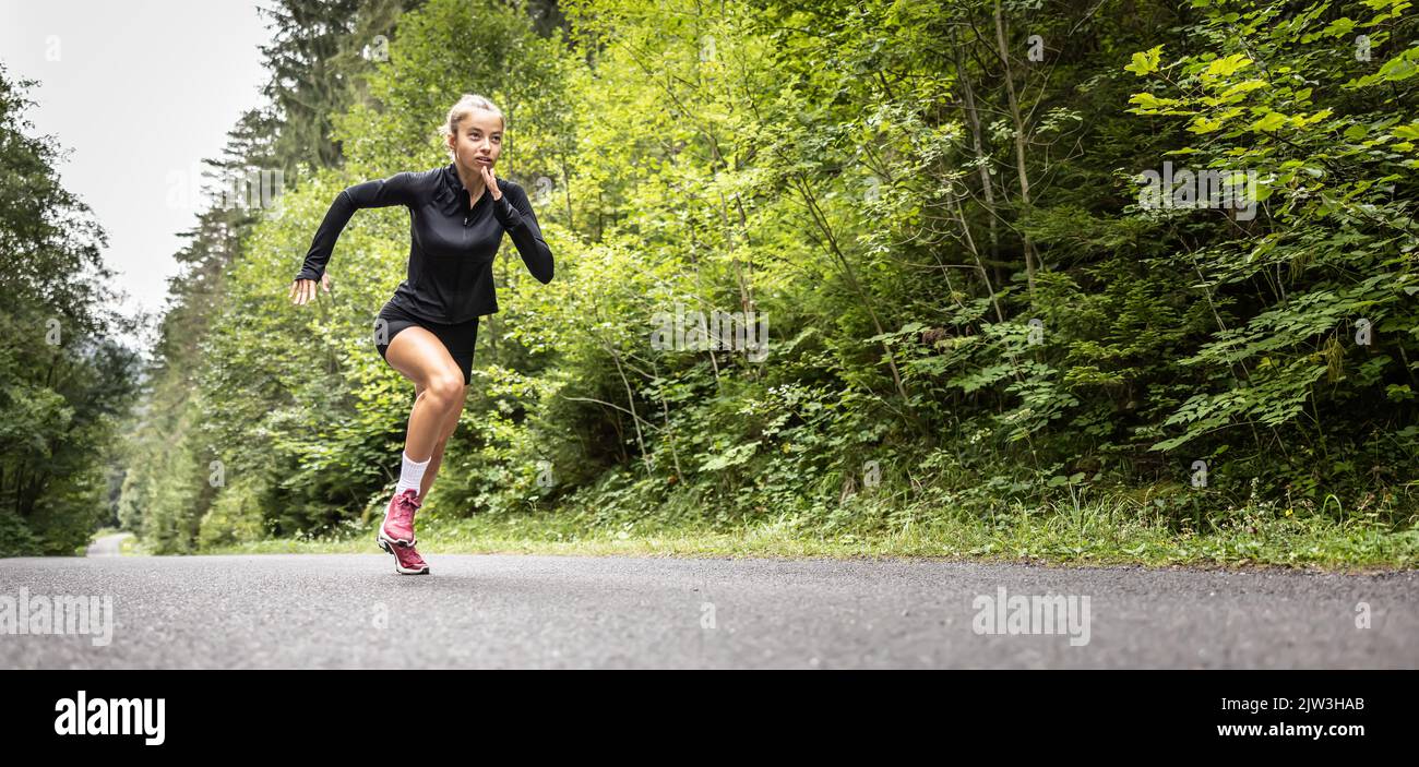 Female athlete starts with an explosive sprint on an asphalt road in ...