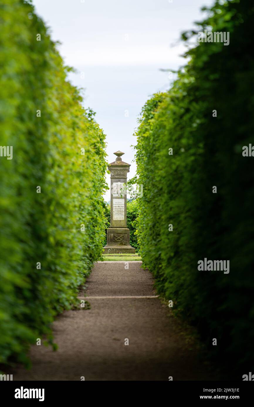 A park path between aligned green trees and a tower at the end of the ...