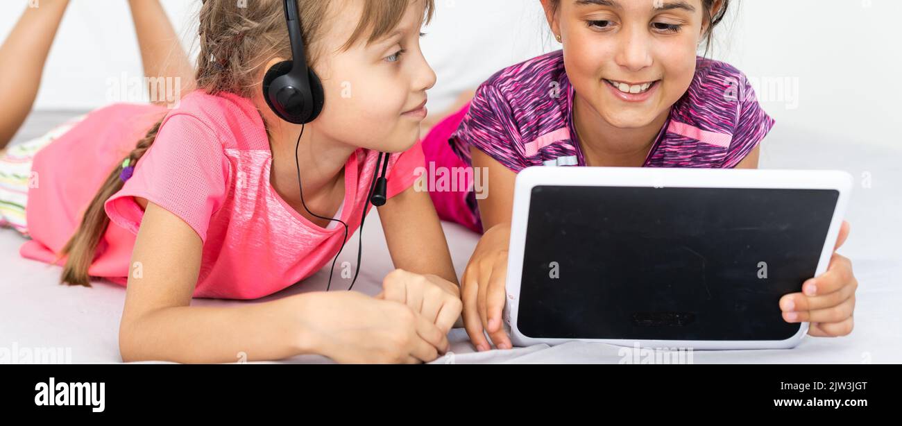 Two cute little girls are using a digital tablet and smiling while ...