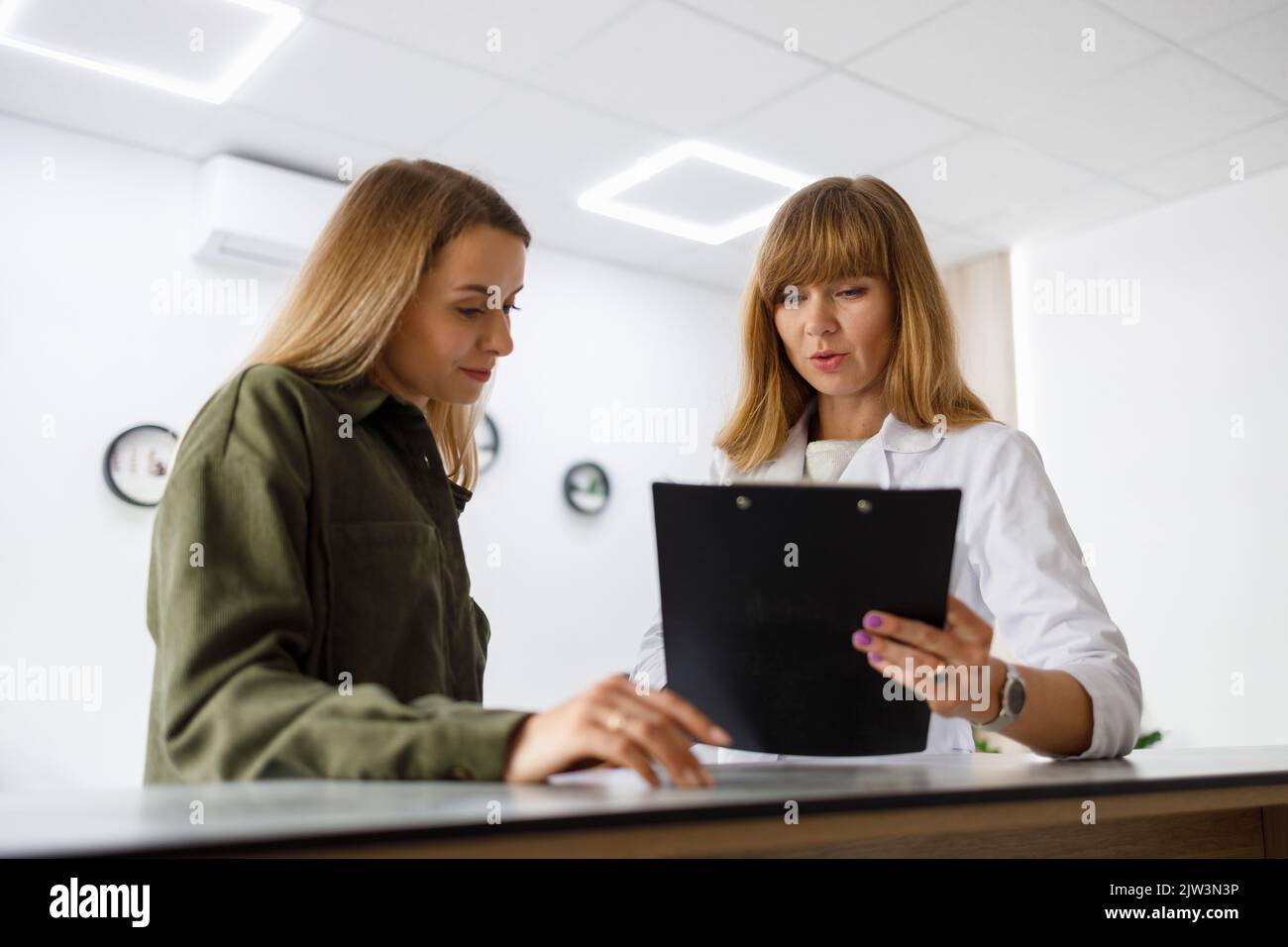 Medical receptionist gives forms to fill to female patient who standing ...