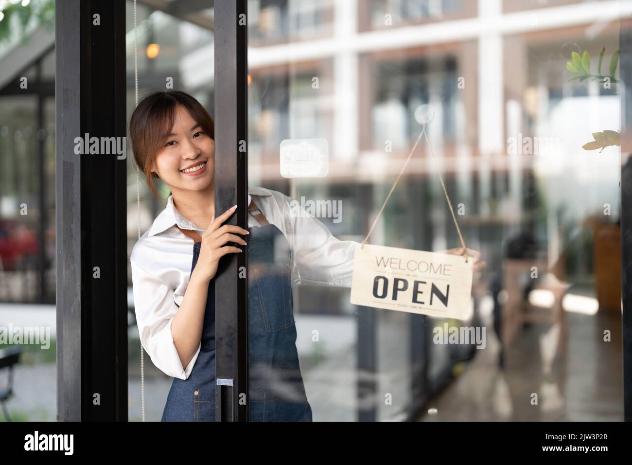 Beautiful asian young barista woman in apron holding tablet and ...