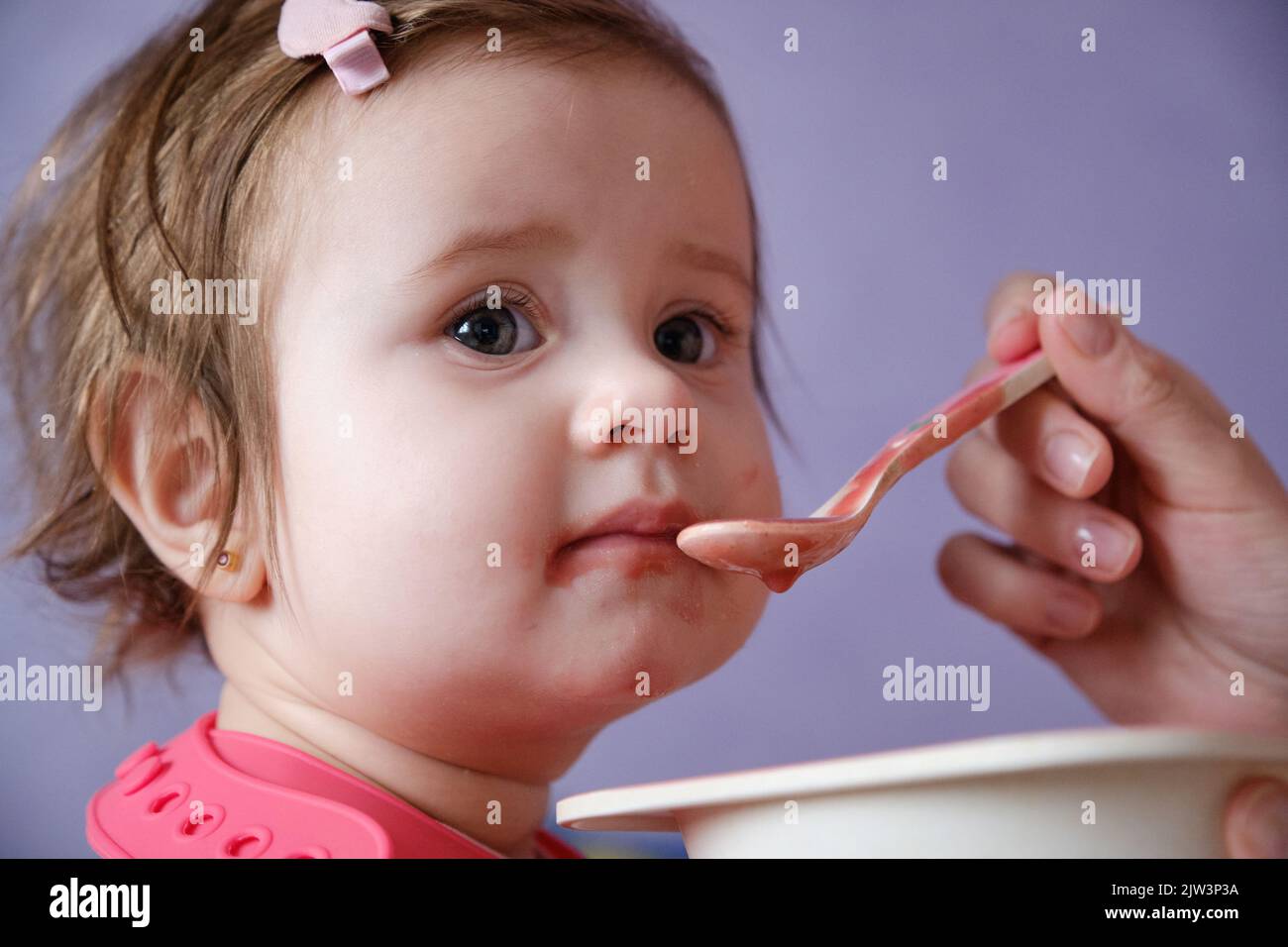 One year old baby girl eating soup. Mother gives baby food from a spoon ...