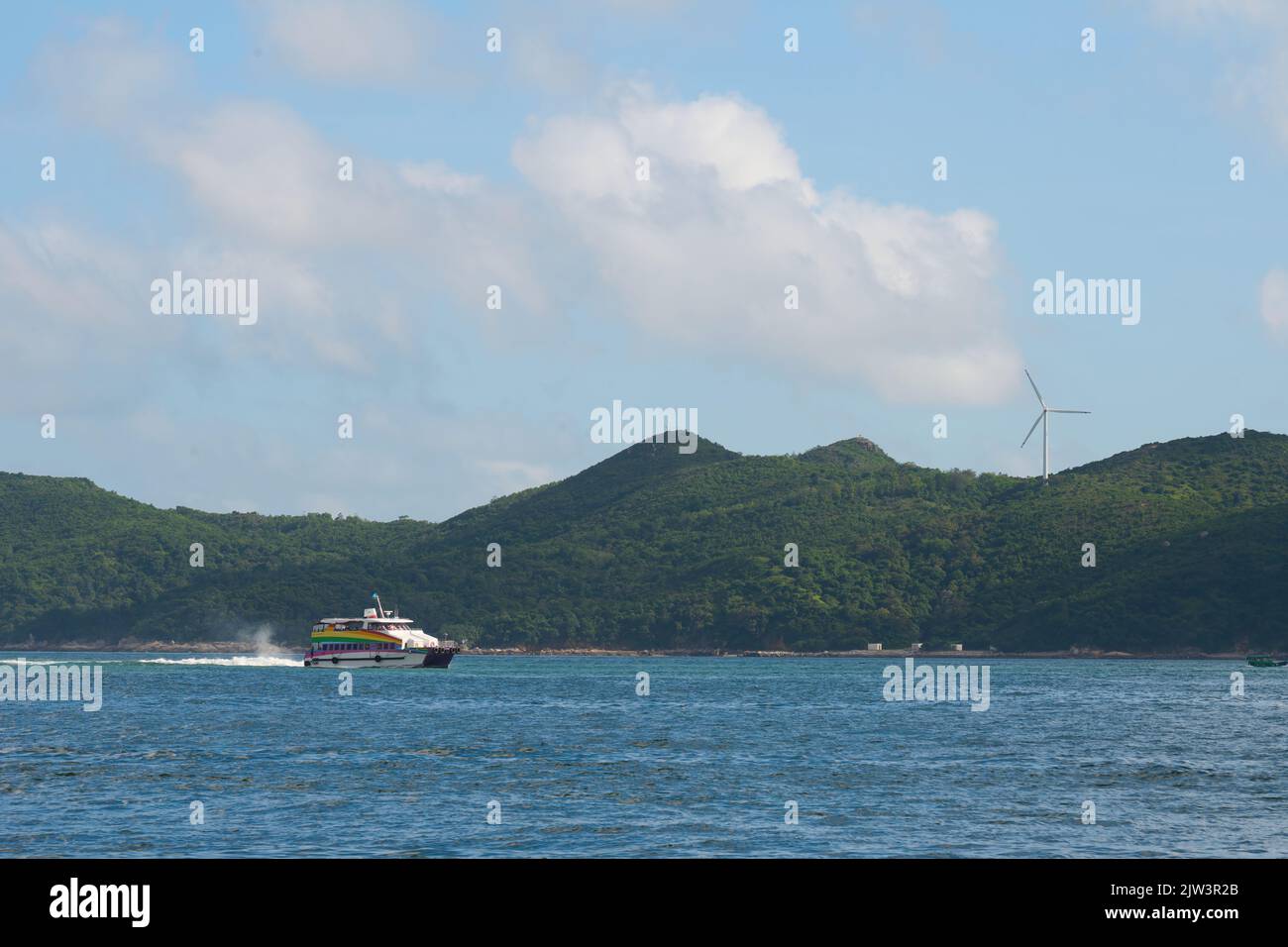 A wind turbine behind the water with a sailing boat in Lamma Island ...