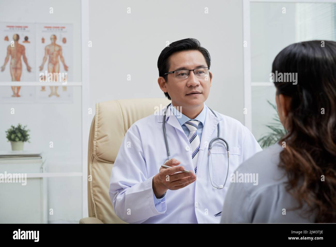 Experienced Vietnamese doctor consulting female patient in his office ...