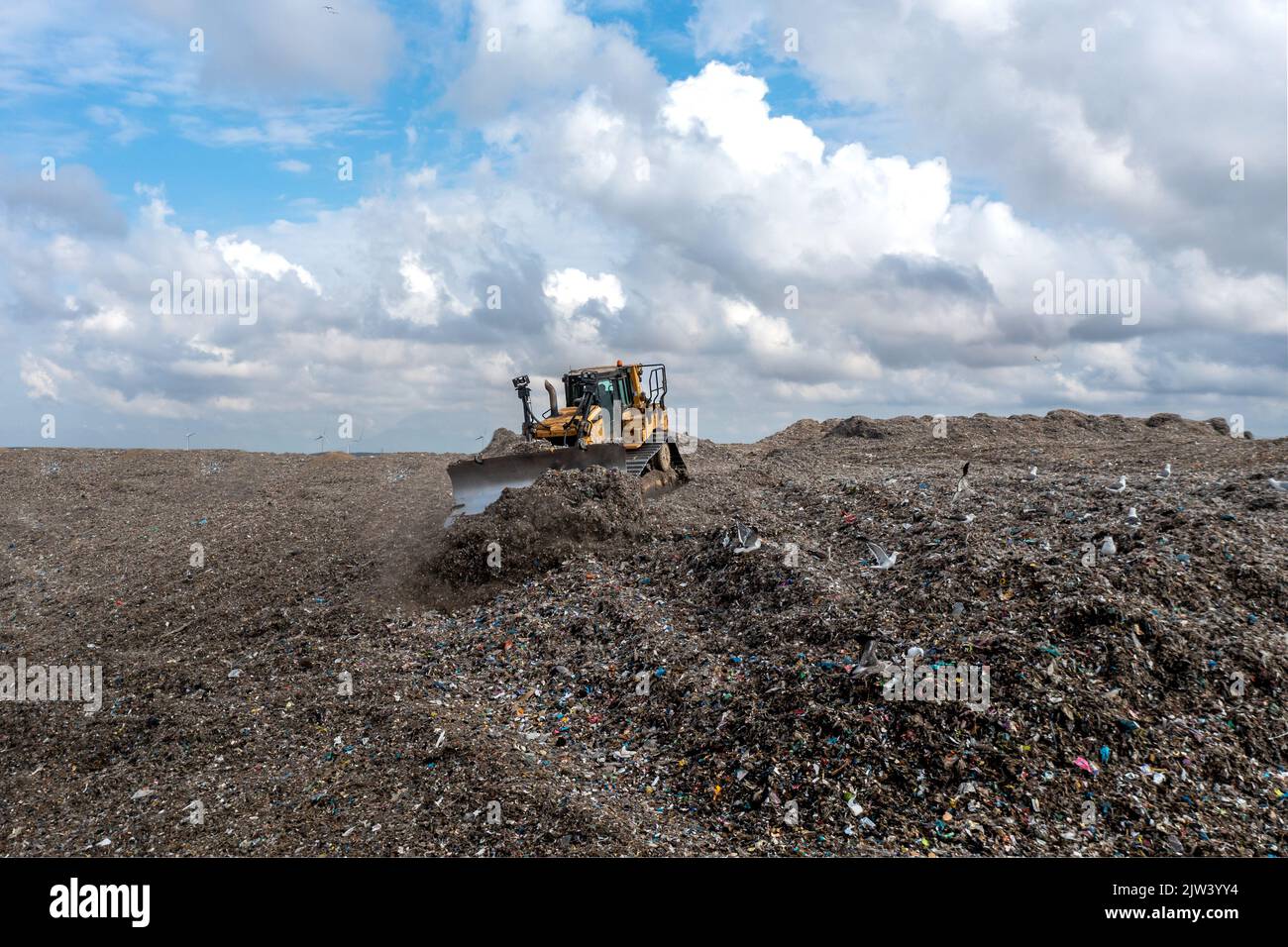 A Bulldozer machine moving waste and household garbage on a large ...