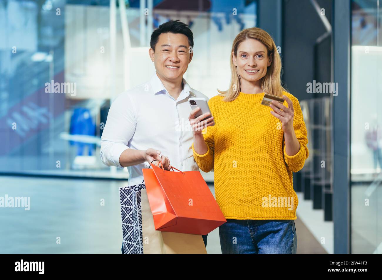 Portrait of happy shoppers asian man and blonde woman smiling and ...