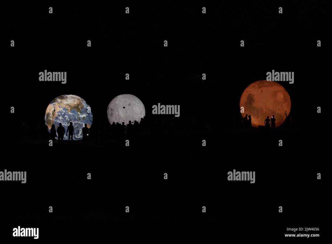 silhouettes of people in front of illuminated models of the Earth, Mars ...