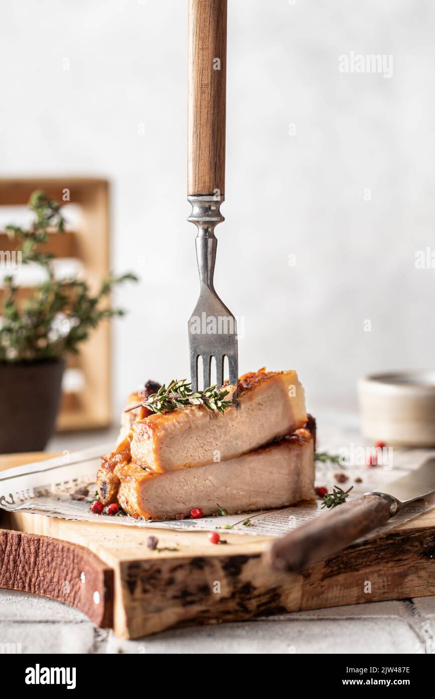 Grilled pork steak sliced with fork on serving board with herbs and ...