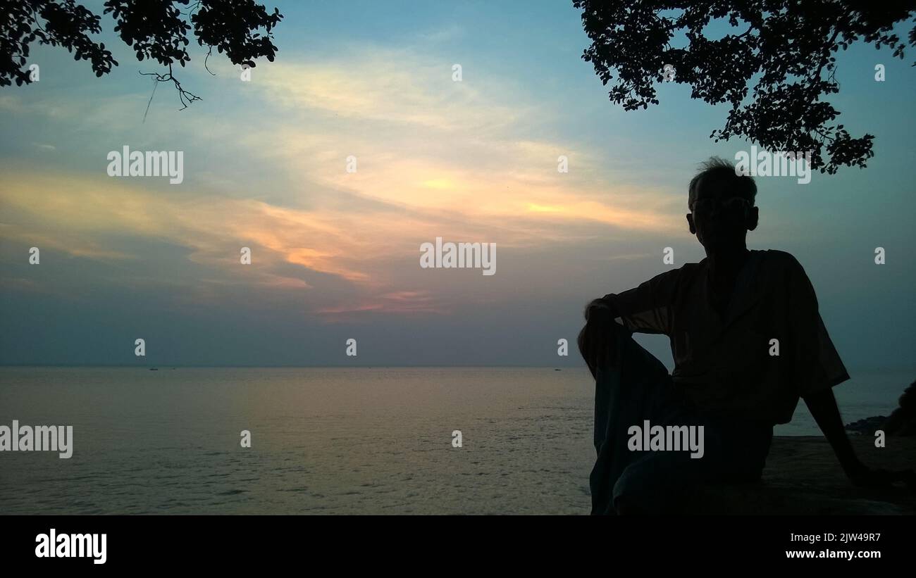 silhouette figure of a an old man relaxing under tree . Colorful sunset ...