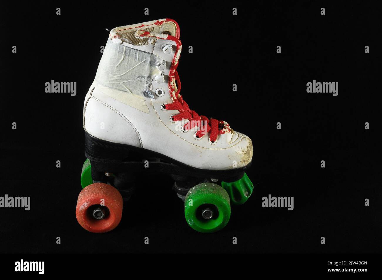 A shot of a used small white roller skate with green and red wheels on ...