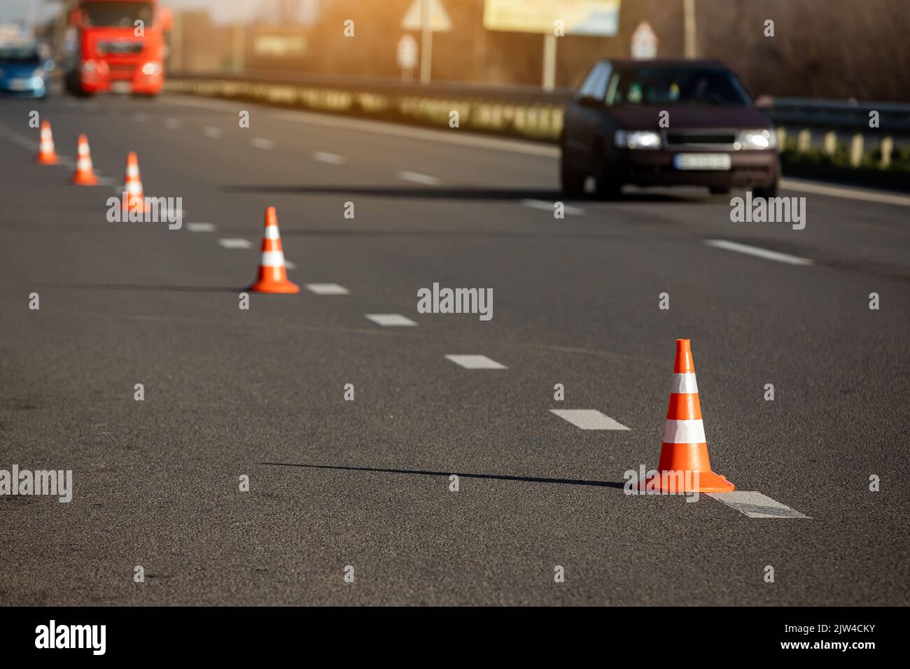 A row of traffic orange striped cones on the road. sunlight. These ...