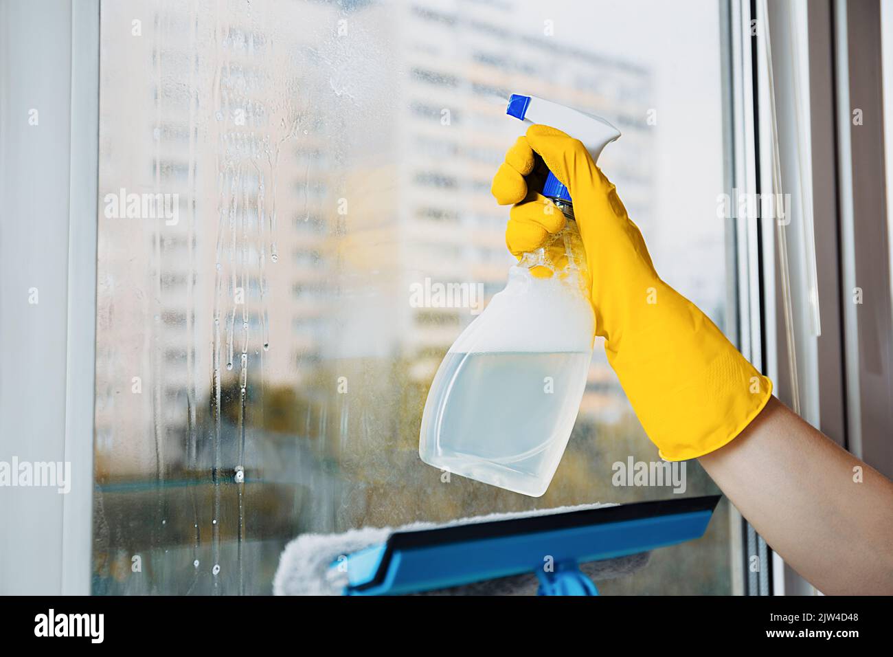 Man in yellow gloves cleaning window with squeegee and spray detergent ...