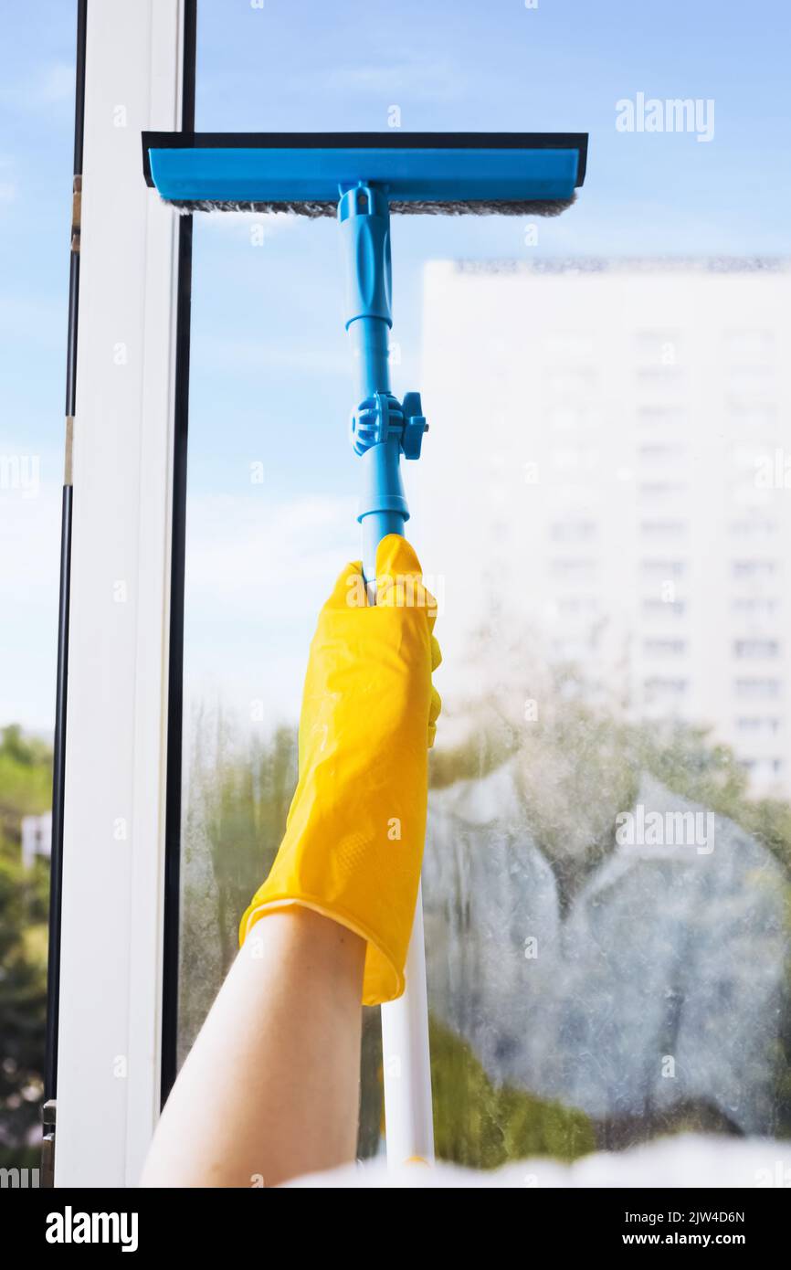 Man in yellow gloves cleaning window with squeegee and spray detergent ...