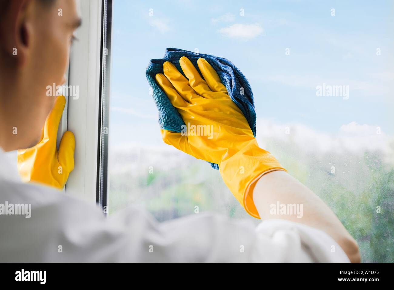 Man in yellow gloves cleaning window with rag and spray detergent at ...