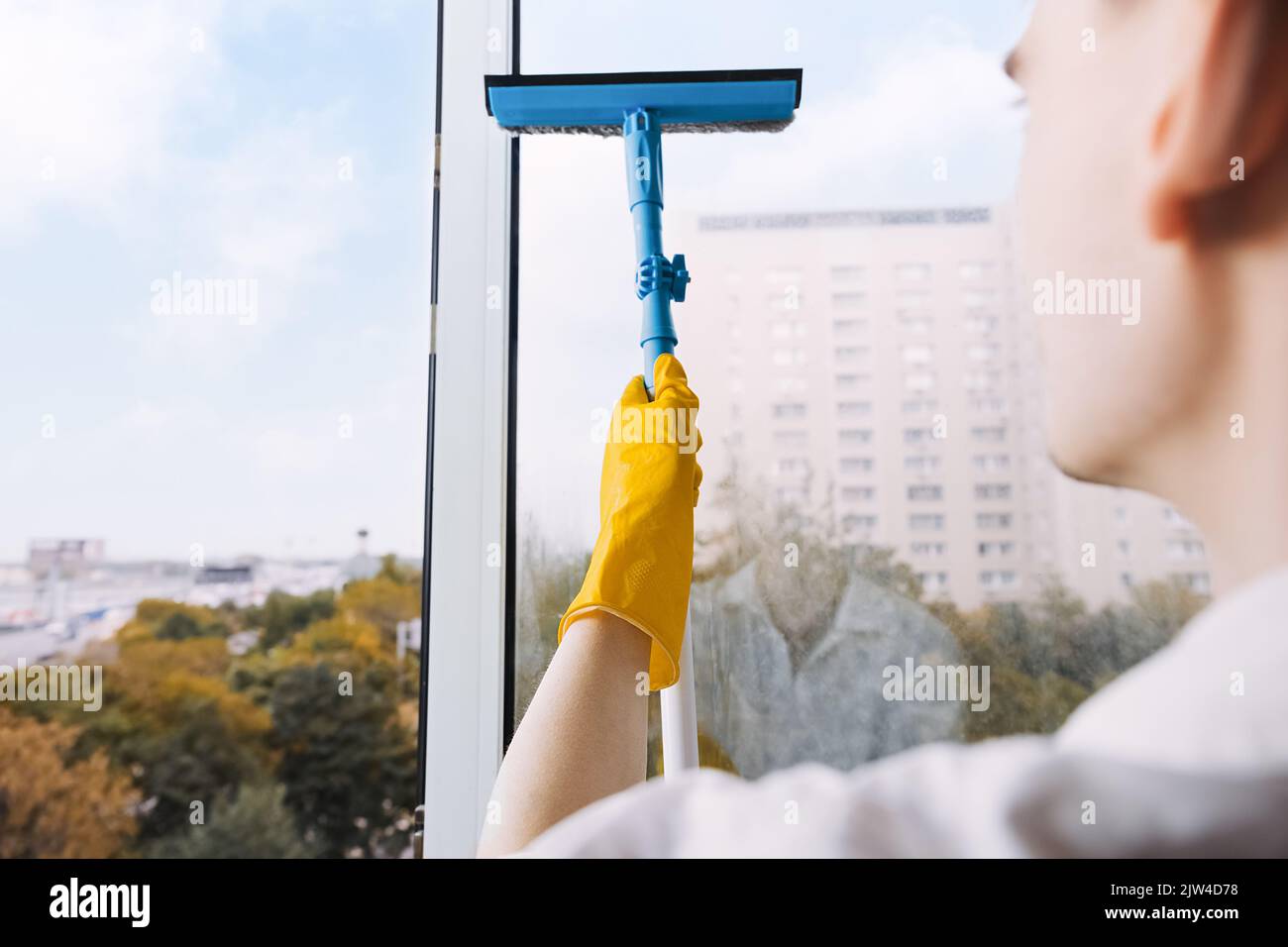 Man in yellow gloves cleaning window with squeegee and spray detergent ...
