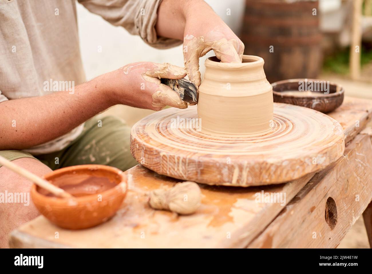 male master in light linen shirt craftsman sculpts jug or vase from ...