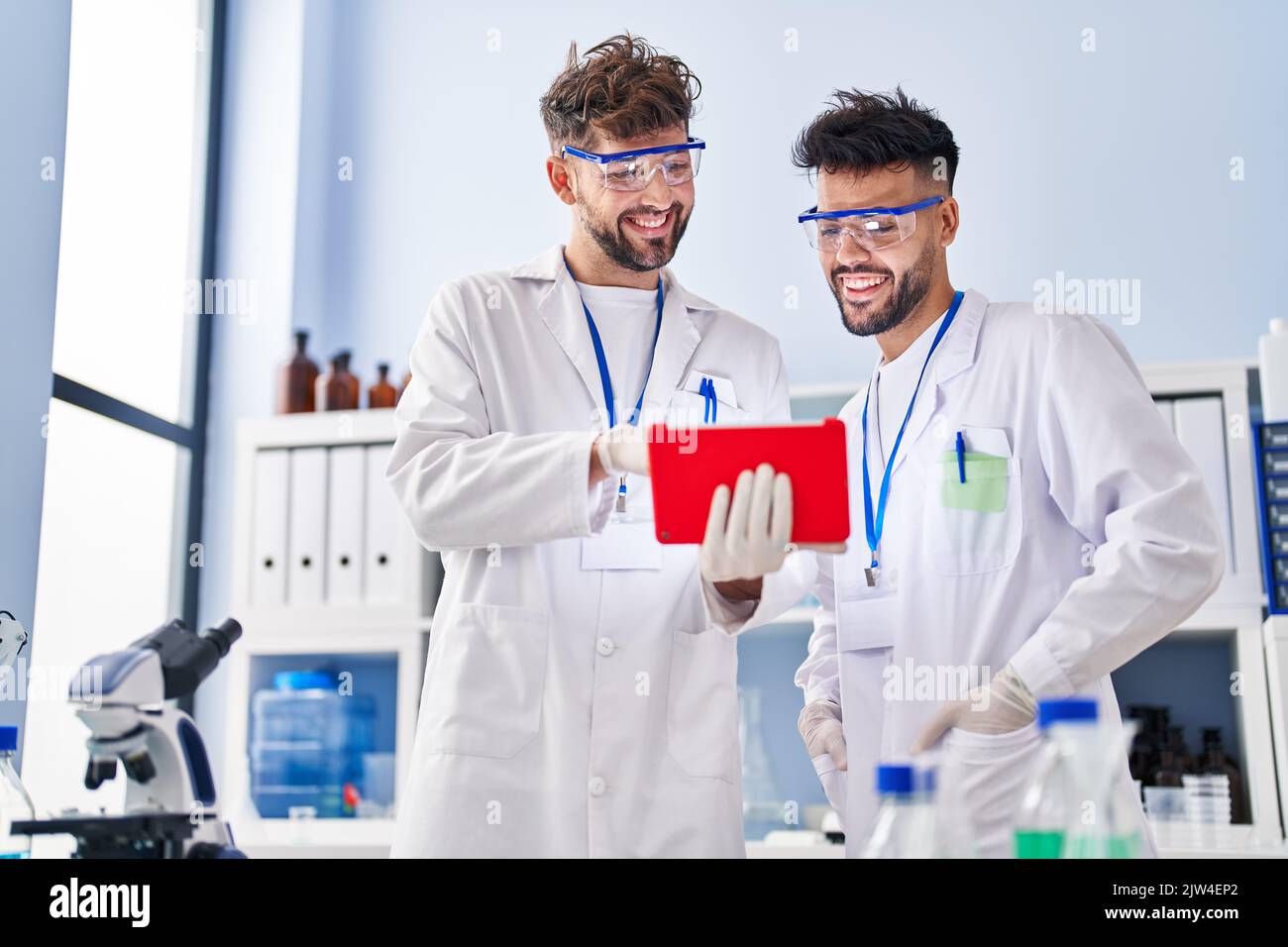 Young couple wearing scientist uniform using touchpad at laboratory ...