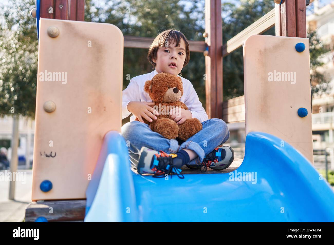 Down syndrome kid smiling confident playing with teddy bear on slide at park Stock Photo - Alamy