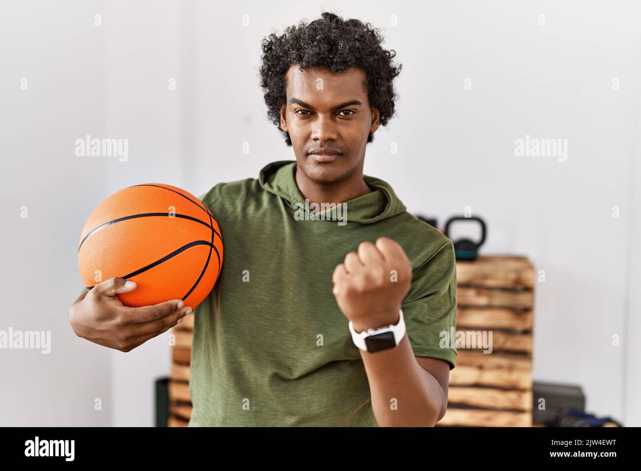 African man with curly hair holding basketball ball at the gym annoyed ...
