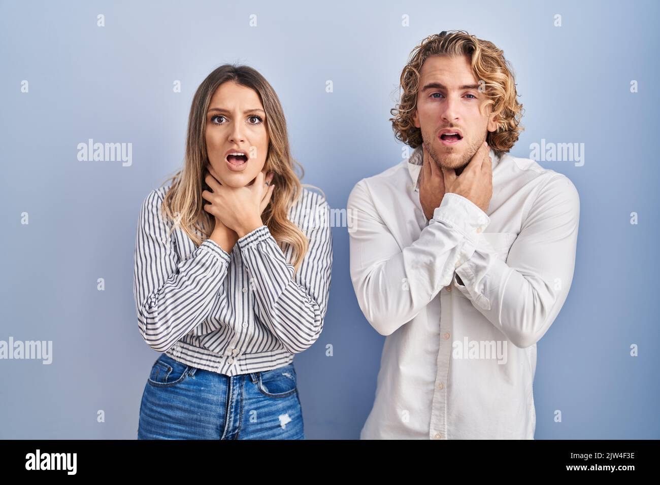 Young couple standing over blue background shouting suffocate because ...