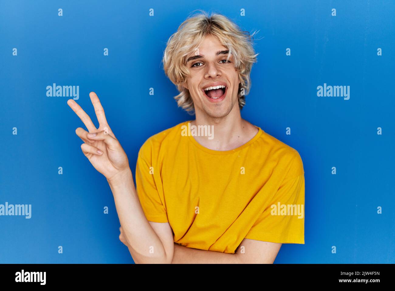 Young modern man standing over blue background smiling with happy face ...