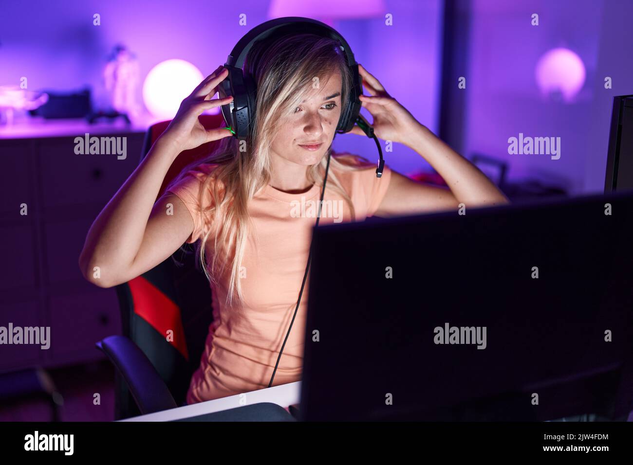 Young blonde woman streamer playing video game using computer at gaming ...