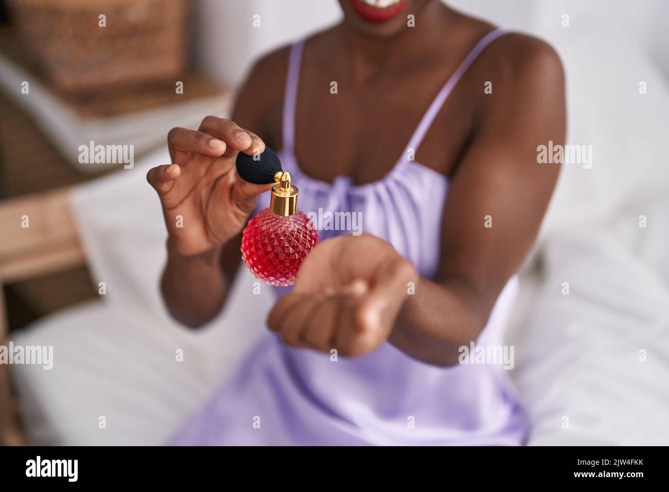 African american woman using perfume sitting on bed at bedroom Stock ...