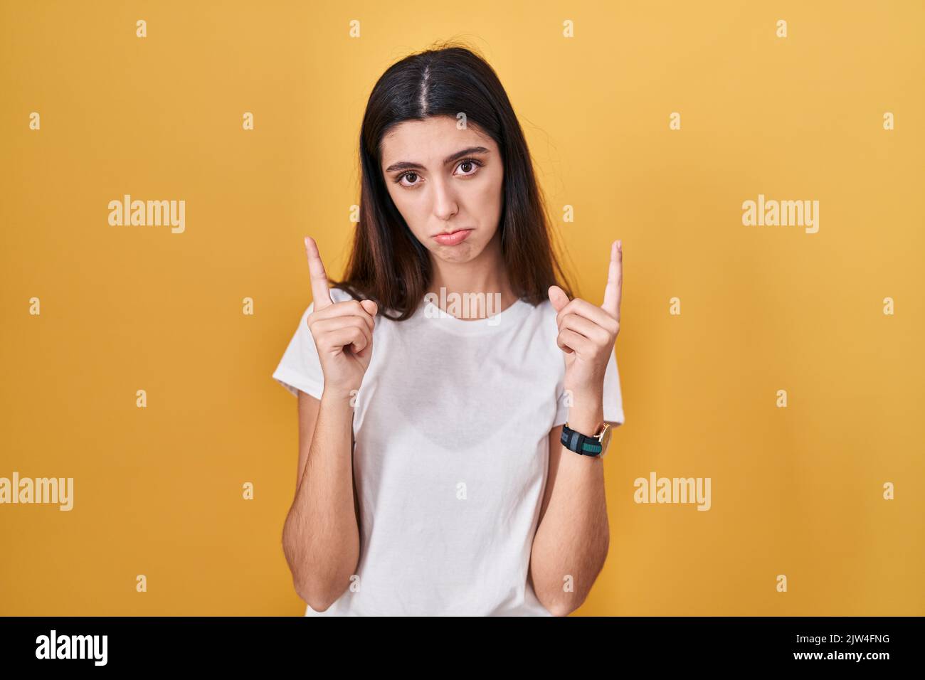 Young beautiful woman standing over yellow background pointing up ...