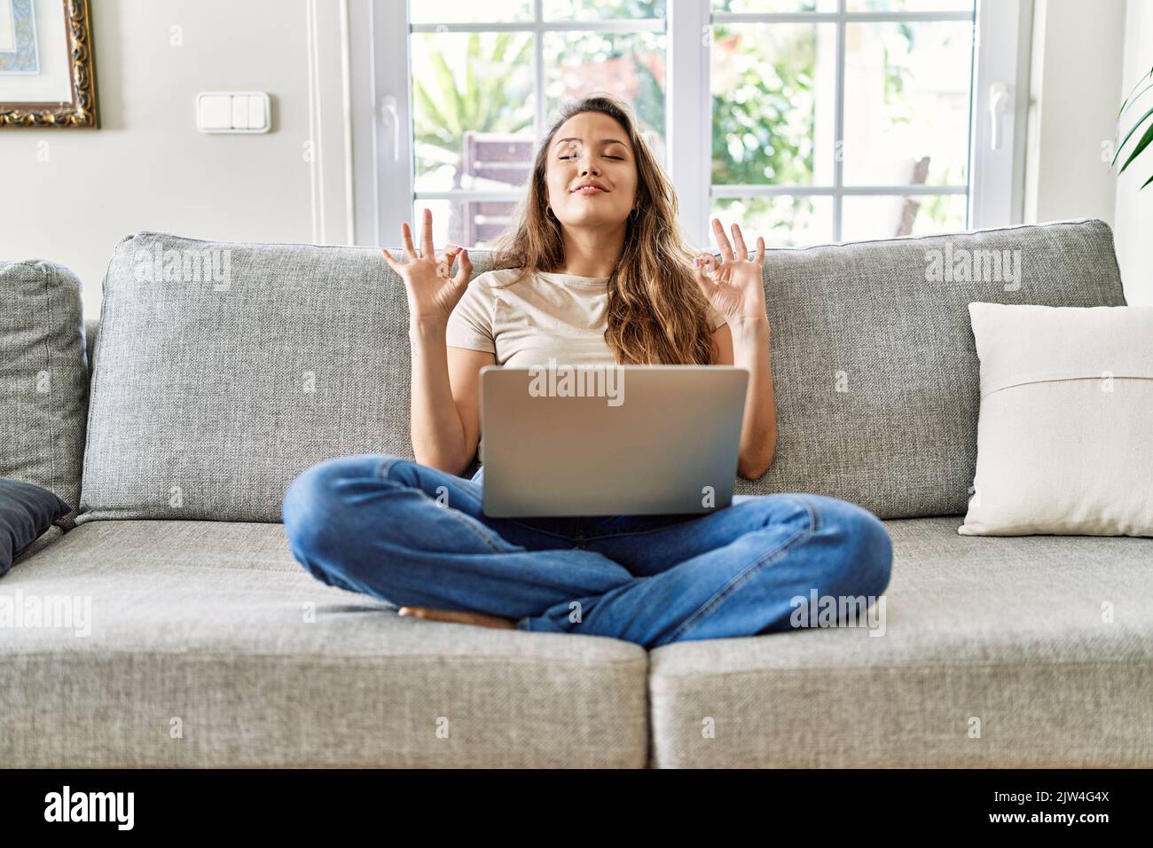 Beautiful young brunette woman sitting on the sofa using computer ...