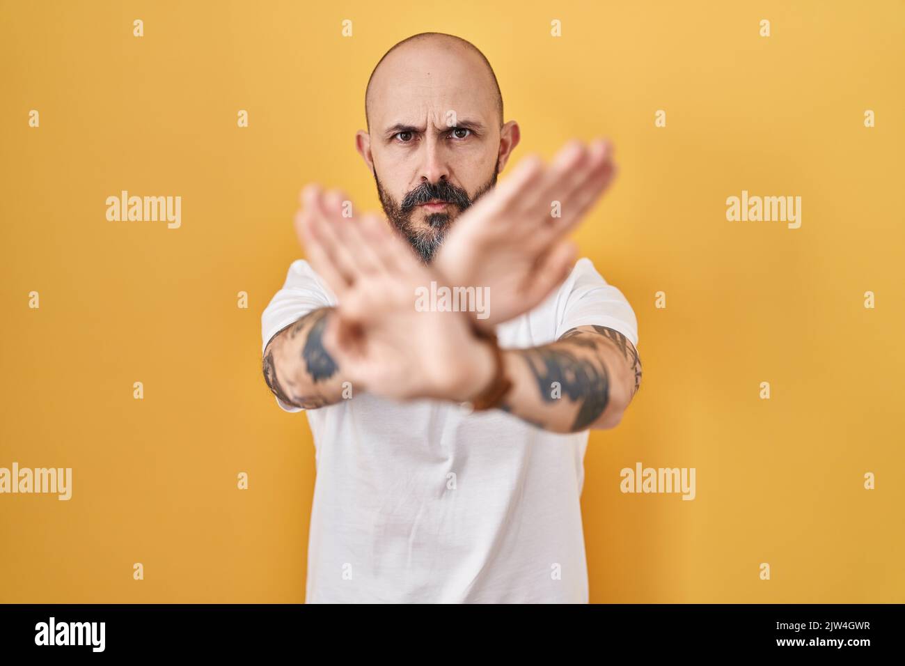 Young hispanic man with tattoos standing over yellow background ...